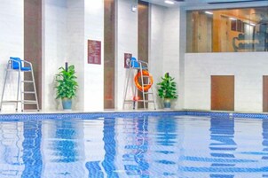 Piscina interior com água cristalina, cercada por paredes com painéis verticais e plantas em vasos.