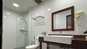 Uma casa de banho moderna com cabine de duche em vidro, sanita branca, lavatório com bancada de mármore e espelho com moldura de madeira.