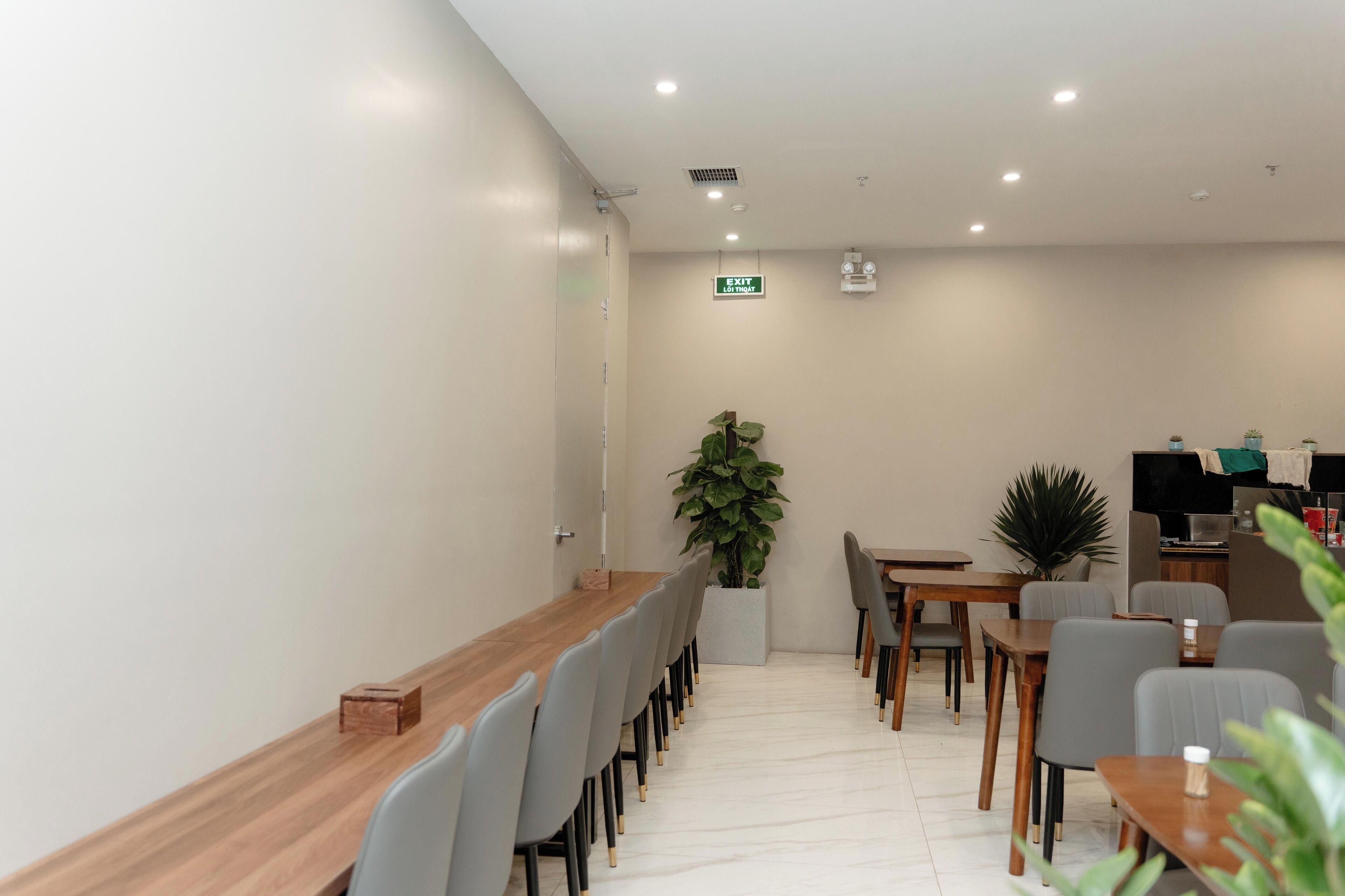 Uma sala de conferências com uma longa mesa de madeira, cadeiras cinzas e um vaso de plantas.