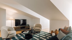 Uma sala de estar moderna com televisão de tela plana, duas poltronas, uma mesa de centro e um sofá.