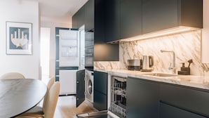 Uma cozinha moderna com armários escuros, bancada de mármore, máquina de lavar louça embutida e cafeteira.
