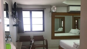 Quarto de hotel pequeno com uma cama, uma mesinha com cadeiras, um espelho e uma janela.