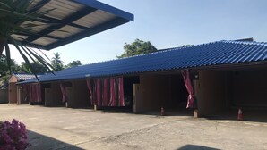 Fileira de edifícios térreos com portas numeradas, área coberta com telhado metálico e chão de concreto.