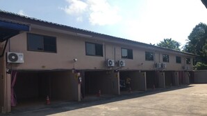 Linha de seis quartos de hotel numerados, com aparelhos de ar condicionado, um extintor de incêndio e uma pessoa em um dos quartos.