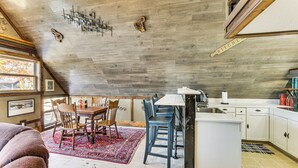 Cozinha com teto de madeira, área de jantar com cadeiras e mesa, e placa de cozinha.