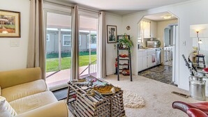 Sala de estar com sofá, mesa de centro com objetos decorativos, cozinha com fogão e porta de vidro deslizante que dá para um pátio.