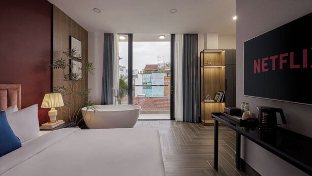 Quarto de hotel moderno com uma cama grande, banheira, televisão e vista para a paisagem urbana.