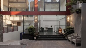 Um edifício moderno de dois andares com grandes janelas de vidro, uma varanda e uma pequena área externa com móveis de vime.