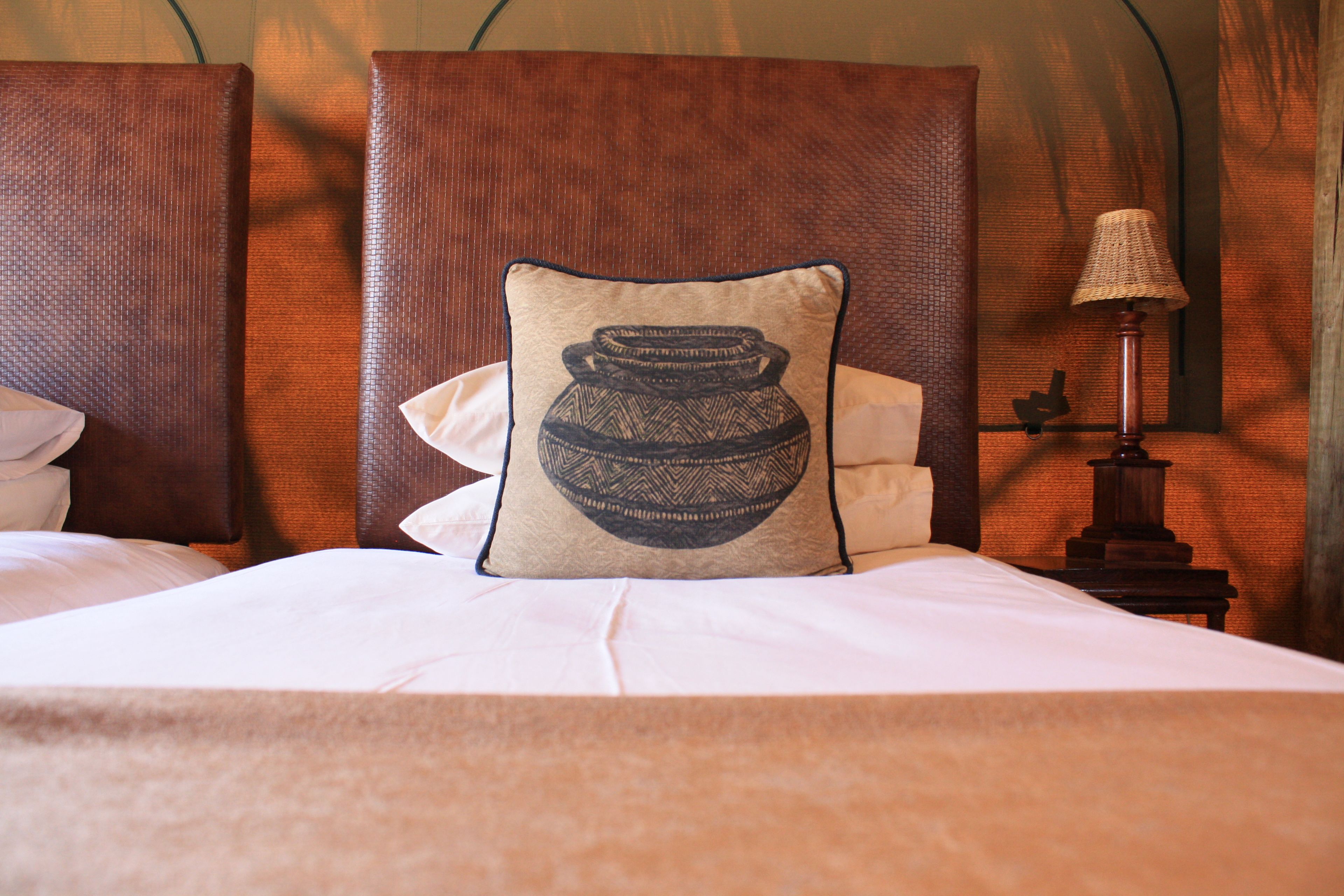 Cama bem arrumada com almofada estampada com um desenho de cerâmica tradicional, luminária sobre uma mesa de cabeceira e cabeceira.