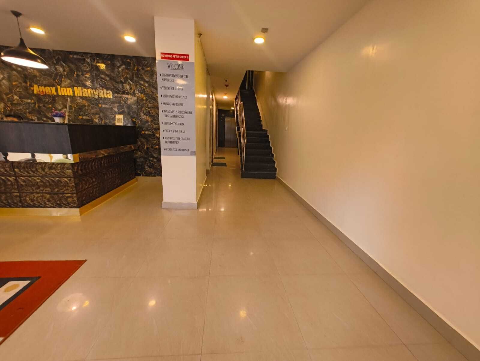 Uma área de recepção de hotel com balcão de mármore, placa de boas-vindas e escadaria para outro andar.