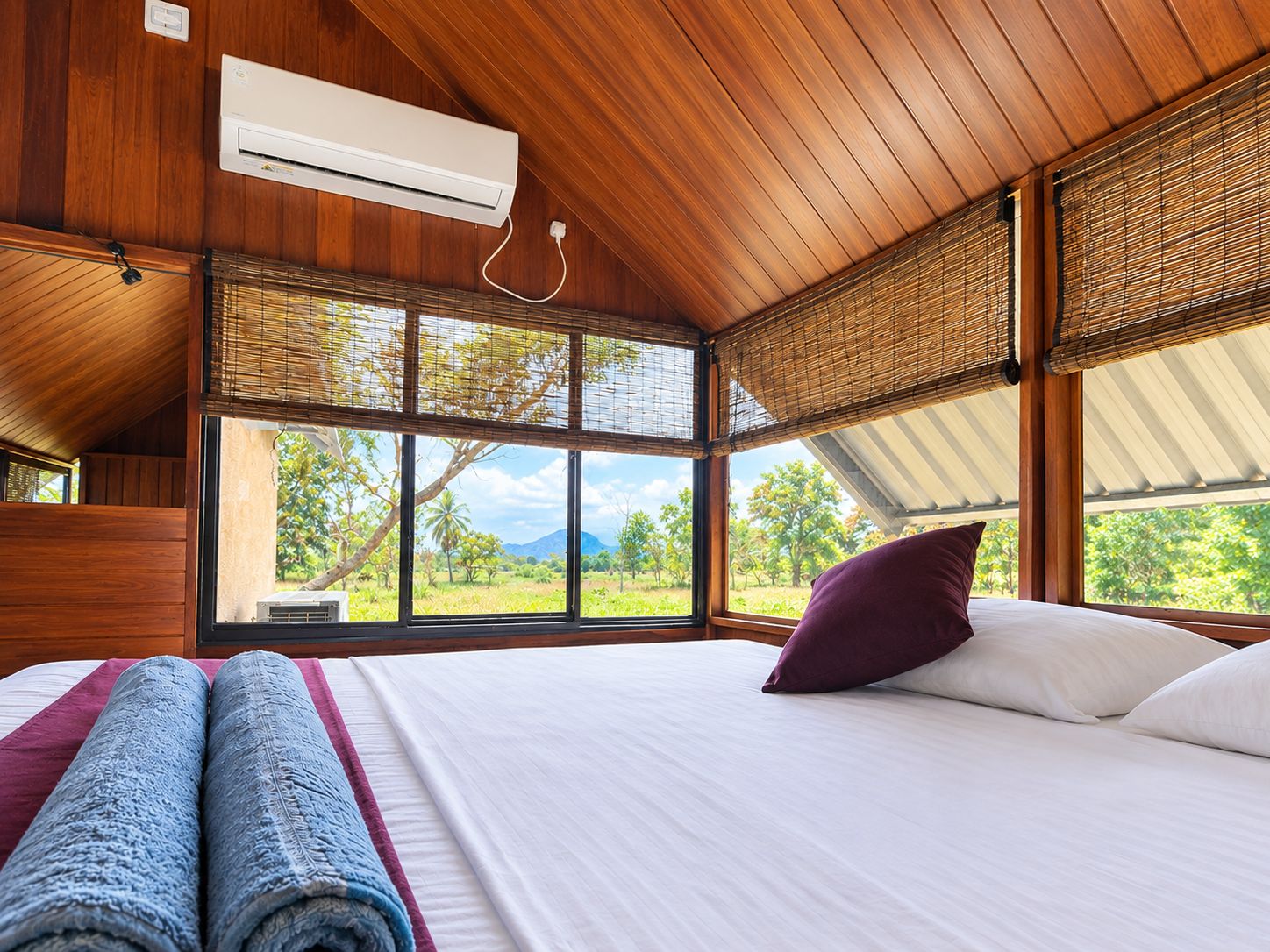 Quarto com cama grande, janela com vista para área verde e ar condicionado.