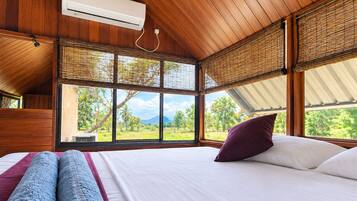 Quarto com cama grande, janela com vista para área verde e ar condicionado.
