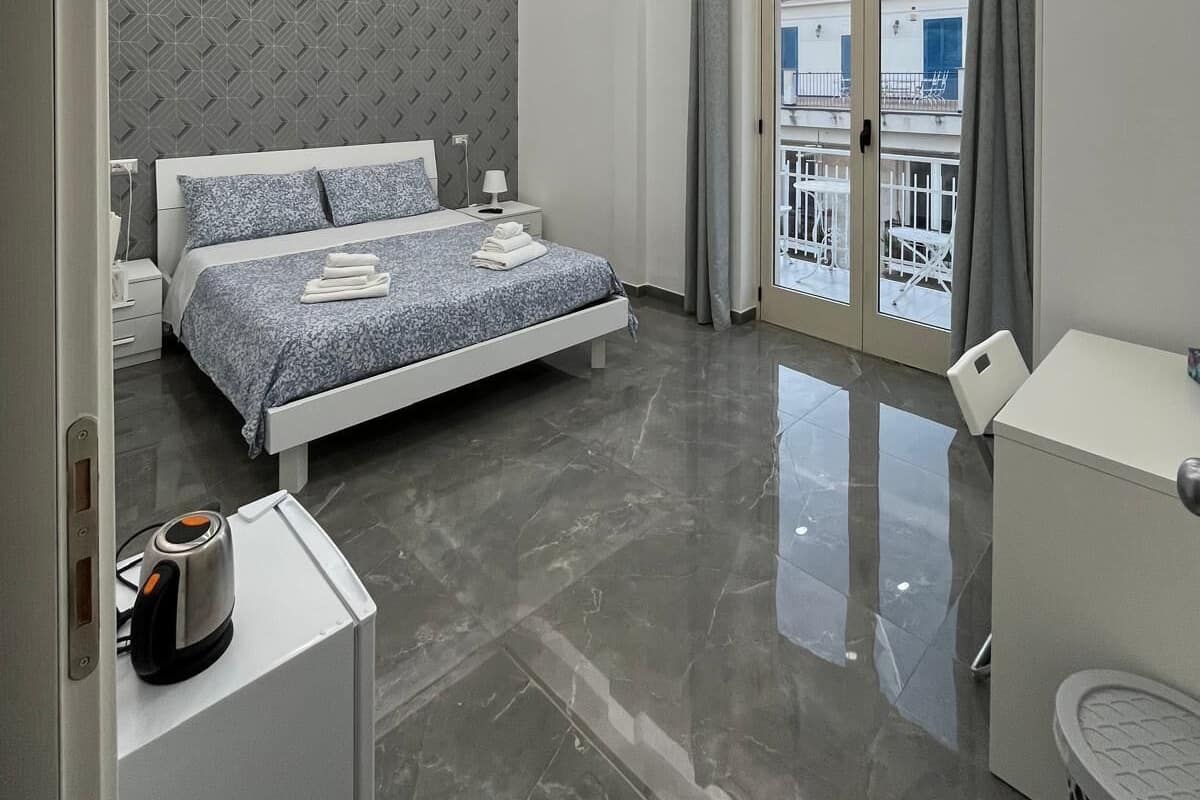 Quarto moderno com cama, mesas de cabeceira, escrivaninha e vista para uma varanda.