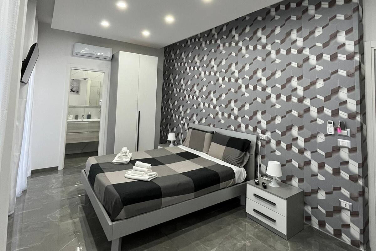 Quarto moderno com cama, mesas de cabeceira e parede estampada.