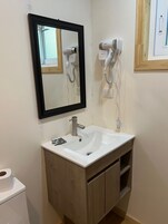 Casa de banho com lavatório branco, espelho, secador de cabelo e sanita.