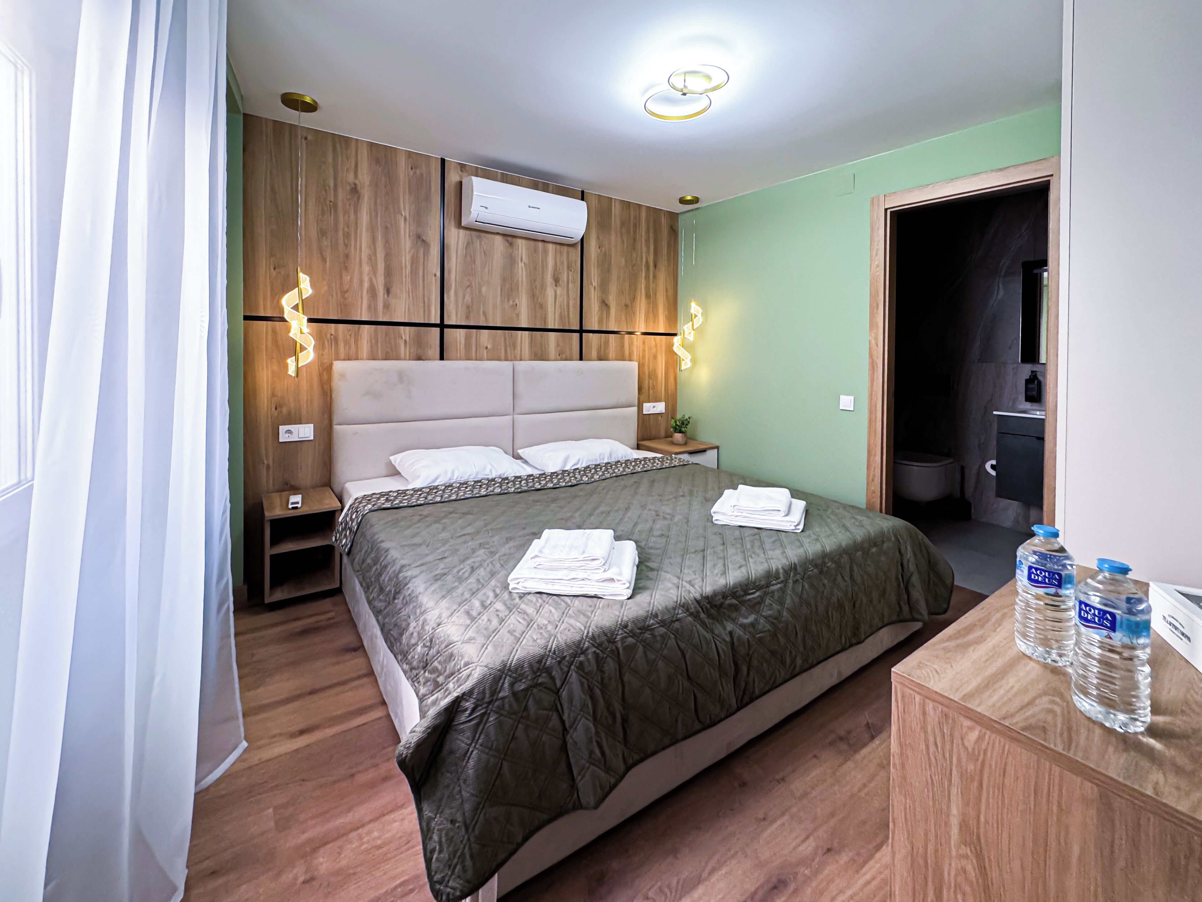 Quarto de hotel com uma cama, mesas de cabeceira, ar condicionado e cabeceira de madeira.