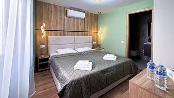 Quarto de hotel com uma cama, mesas de cabeceira, ar condicionado e cabeceira de madeira.