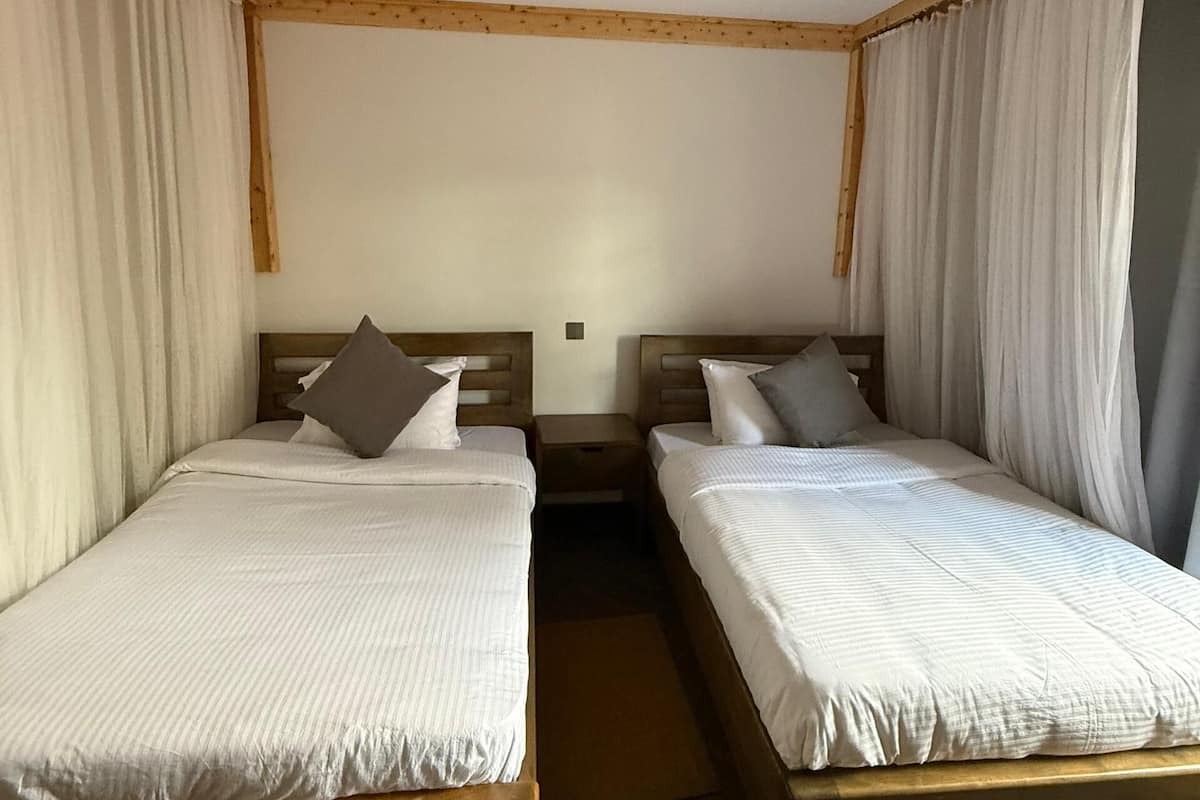 Quarto com duas camas de solteiro, cabeceiras de madeira e piso de madeira.