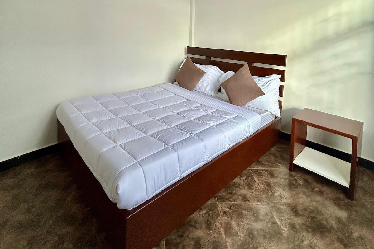 Quarto com cama, cabeceira de madeira e mesa de cabeceira.