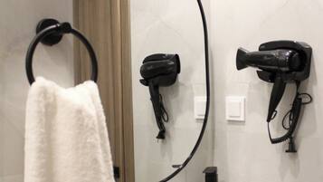 Uma casa de banho com uma pia branca, uma toalha pendurada num suporte e dois secadores de cabelo fixados na parede.