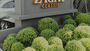 Placa do Hotel Zagat Classic com design moderno, rodeada por arbustos bem cuidados.