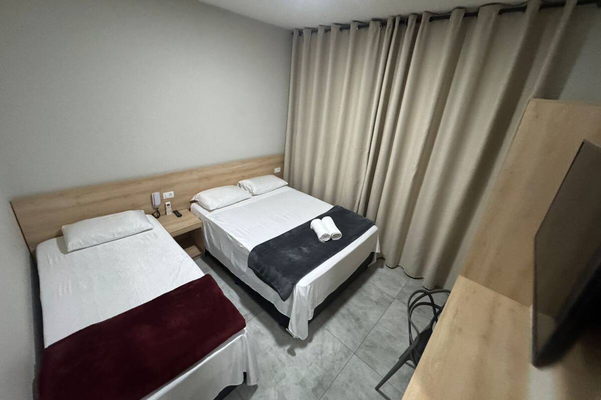 Quarto de hotel com duas camas, uma escrivaninha, uma cadeira e uma televisão.