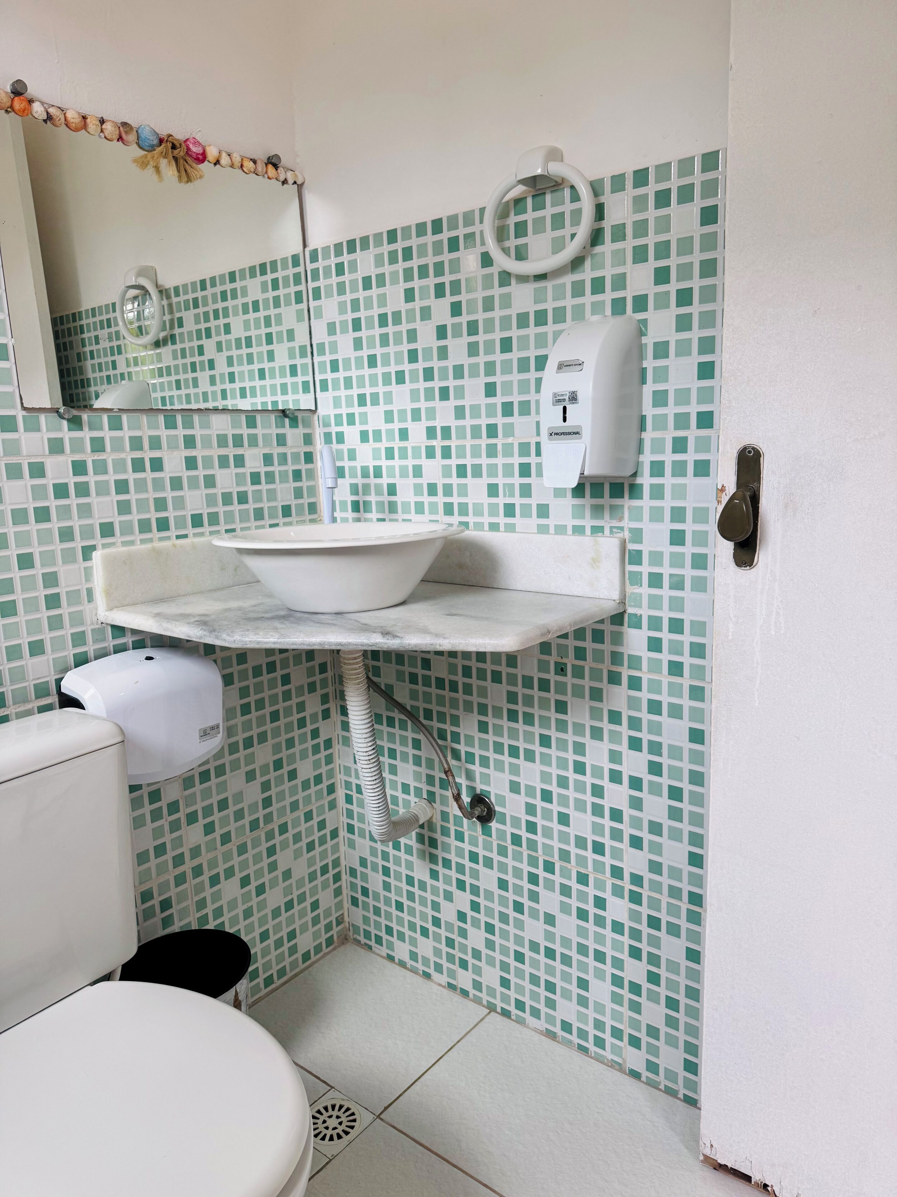 Uma casa de banho com uma pia branca, um espelho, uma sanita e um secador de mãos.