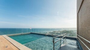 Piscina infinita no terraço com água cristalina, grades de metal e vista para o oceano.