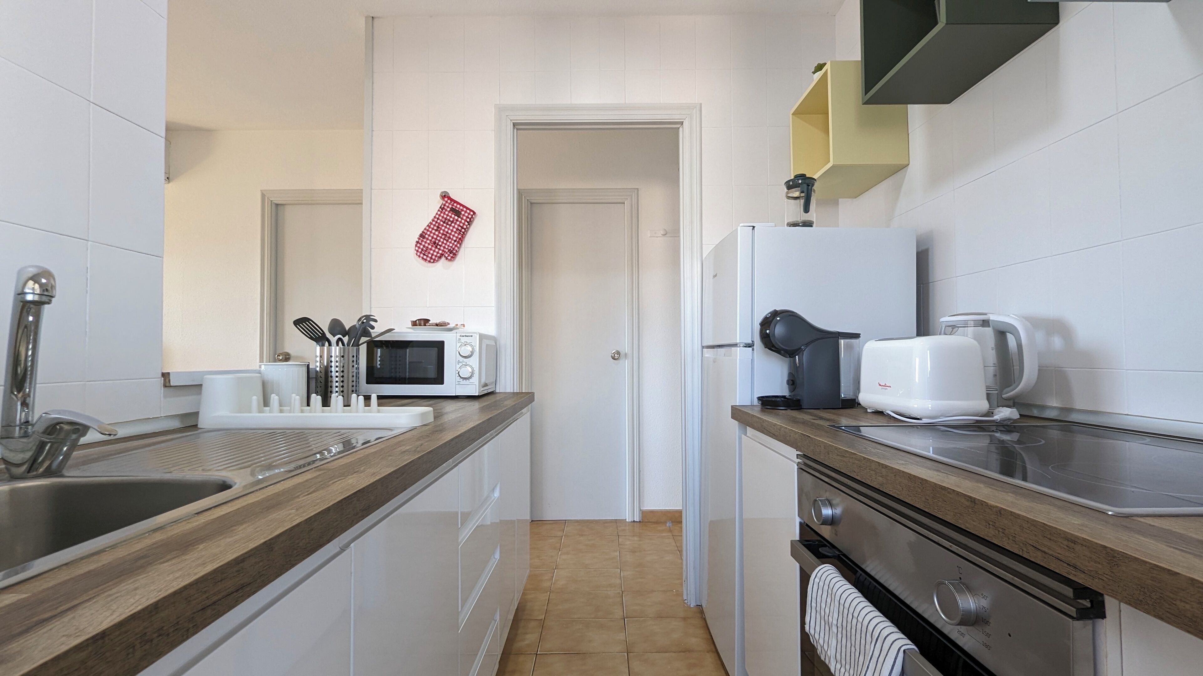 Uma cozinha moderna com micro-ondas, torradeira e chaleira sobre a bancada, pia e porta que dá para outro cômodo.