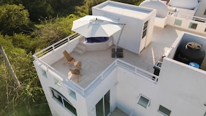 Terraço no telhado com banheira de hidromassagem, uma mesa com cadeiras e um grande guarda-sol.