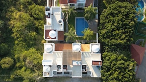 Vista aérea de uma casa moderna com piscina, quadra de tênis e vegetação exuberante ao redor da propriedade.