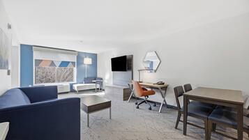 Quarto de hotel moderno com sofá, escrivaninha, cadeira, televisão e janela com vista.