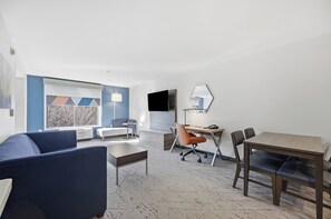 Quarto de hotel moderno com sofá, escrivaninha, cadeira, televisão e janela com vista.