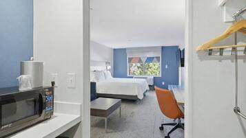 Quarto de hotel com cama, escrivaninha, cadeira, micro-ondas e janela com vista para árvores.