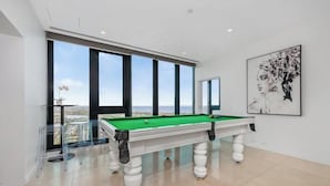 Uma mesa de bilhar em um ambiente com janelas amplas, uma obra de arte emoldurada na parede e vista para o exterior.