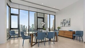 Uma sala de jantar moderna com mesa de vidro, cadeiras azuis e vista para a cidade.