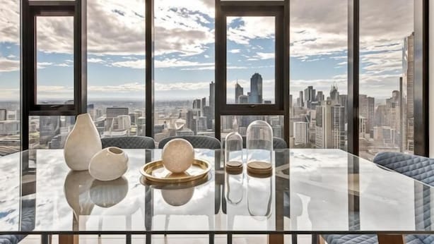 Quarto em um prédio alto, com mesa de vidro, objetos decorativos e vista para a cidade.