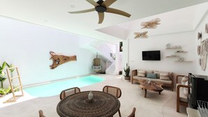 Uma sala de estar espaçosa com piscina, ventilador de teto, TV e área de estar com mesa de centro.