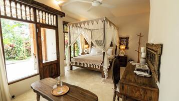 Quarto com cama de dossel, escrivaninha de madeira e vista para o verde lá fora.