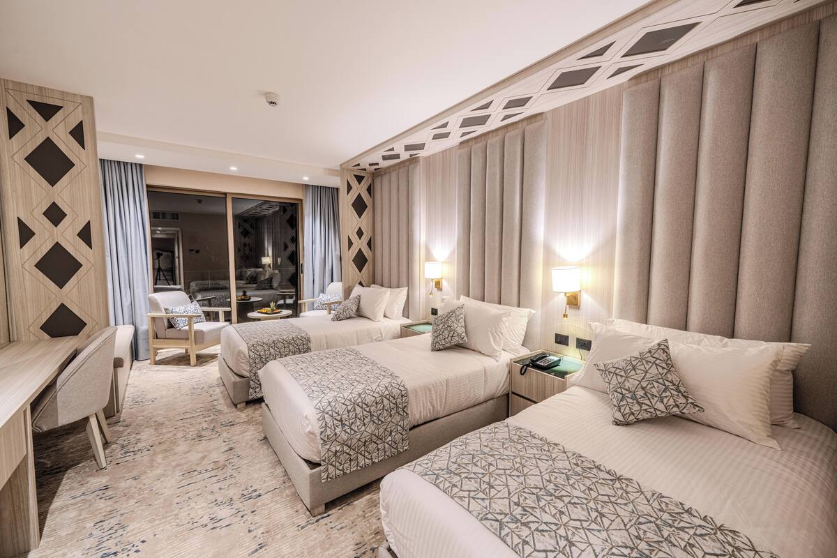 Quarto de hotel com três camas, uma escrivaninha e vista para a cidade.