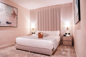 Quarto moderno com cama grande, mesa de cabeceira, luminária na parede e uma pintura.
