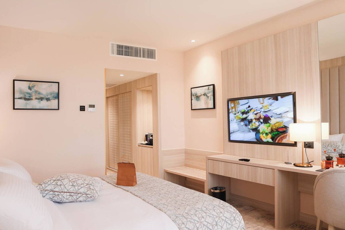 Quarto de hotel moderno com uma cama grande, uma escrivaninha e uma televisão de tela plana, além de obras de arte nas paredes.