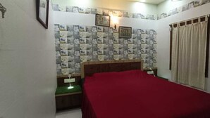 Um quarto com uma cama, uma mesa de cabeceira, uma luminária na parede e uma janela com cortinas.