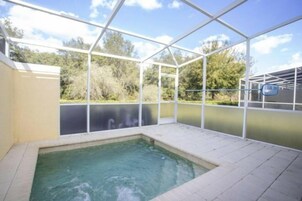 Piscina com cobertura de vidro, rodeada por um deck e vista para árvores.