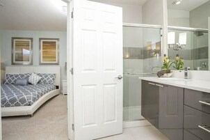 Quarto com cama, banheiro com chuveiro e uma porta branca.