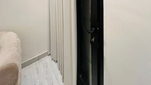 Um corredor com uma porta preta, cortinas brancas e um sofá bege.
