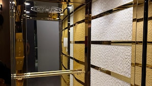 Interior de elevador com paredes refletoras, piso estampado e luminária no teto.