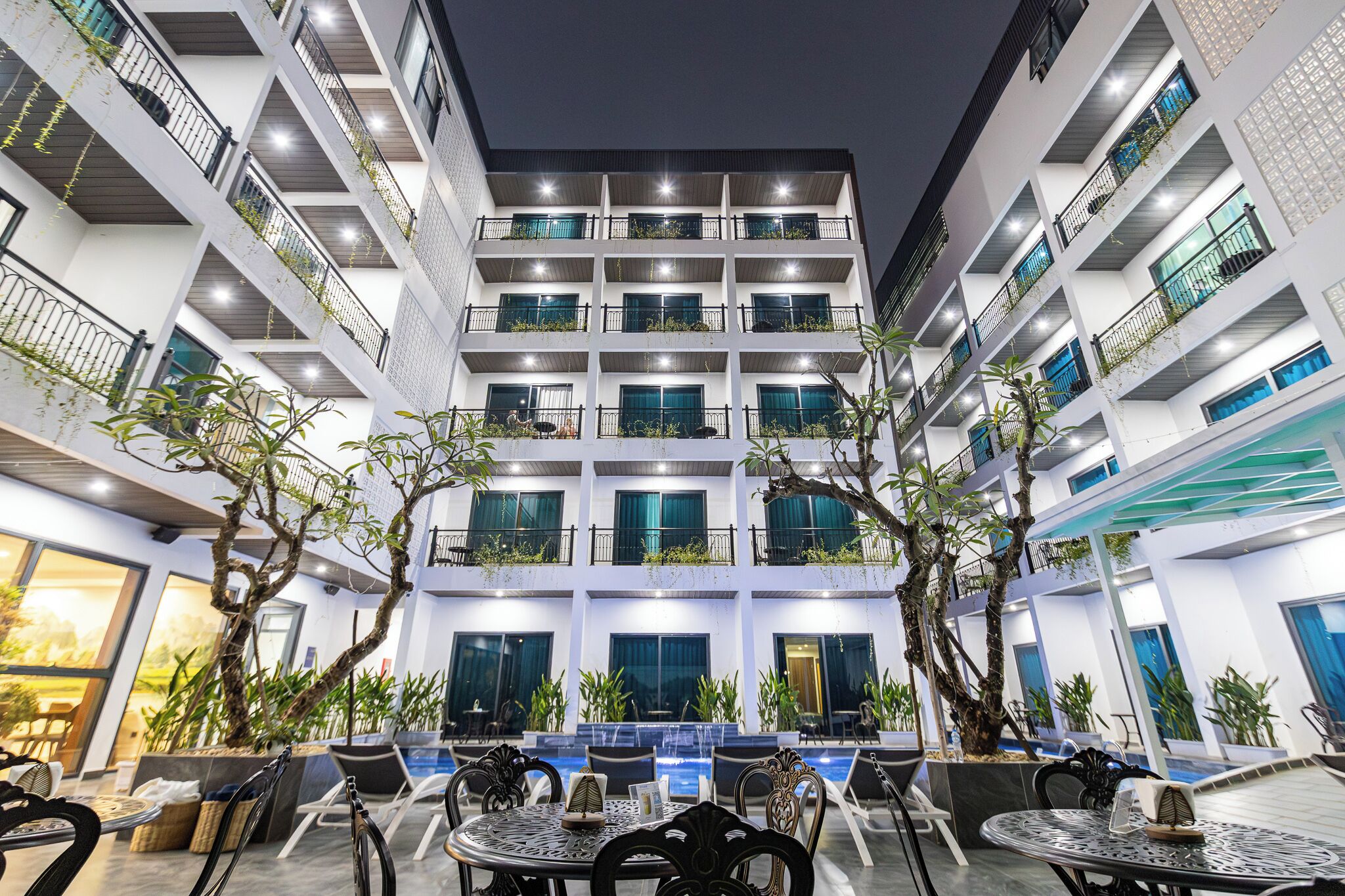 Um hotel com vários andares, áreas de estar ao ar livre, varandas com plantas e janelas grandes.