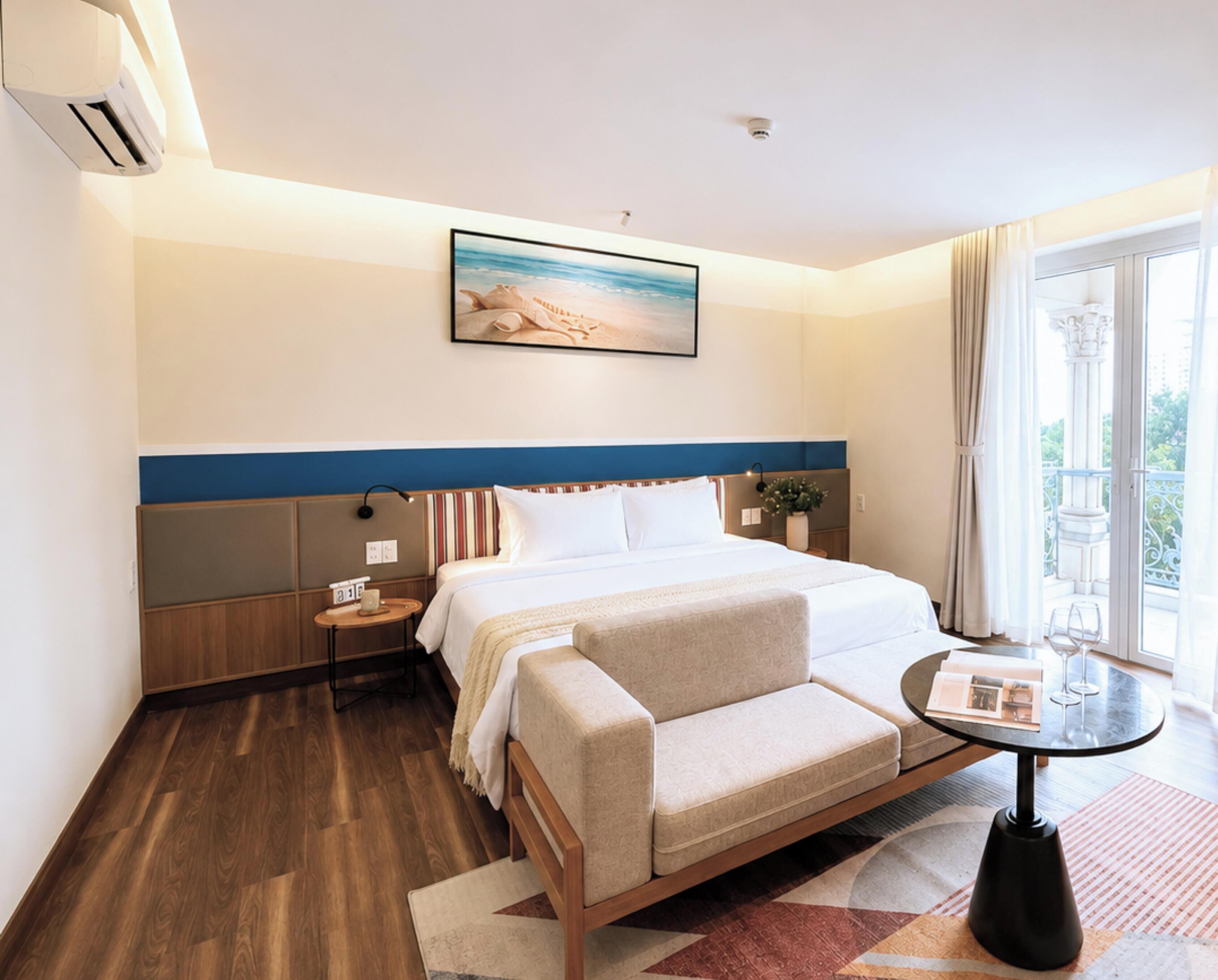 Quarto de hotel com uma cama, mesa de cabeceira, cadeira, pequena mesa com copos e uma janela com cortinas.