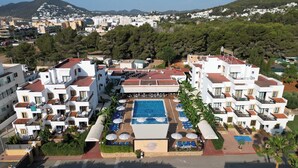 Um hotel com piscina, várias varandas e vista para a cidade e colinas ao redor.